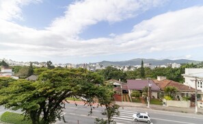 Vista da rua com uma faixa de pedestres, um carro branco e edifícios ao fundo.