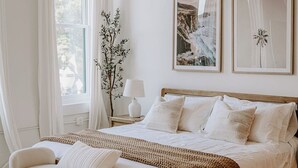 Quarto com uma cama grande, uma mesa de cabeceira com abajur, luminária pendente e duas imagens emolduradas na parede.