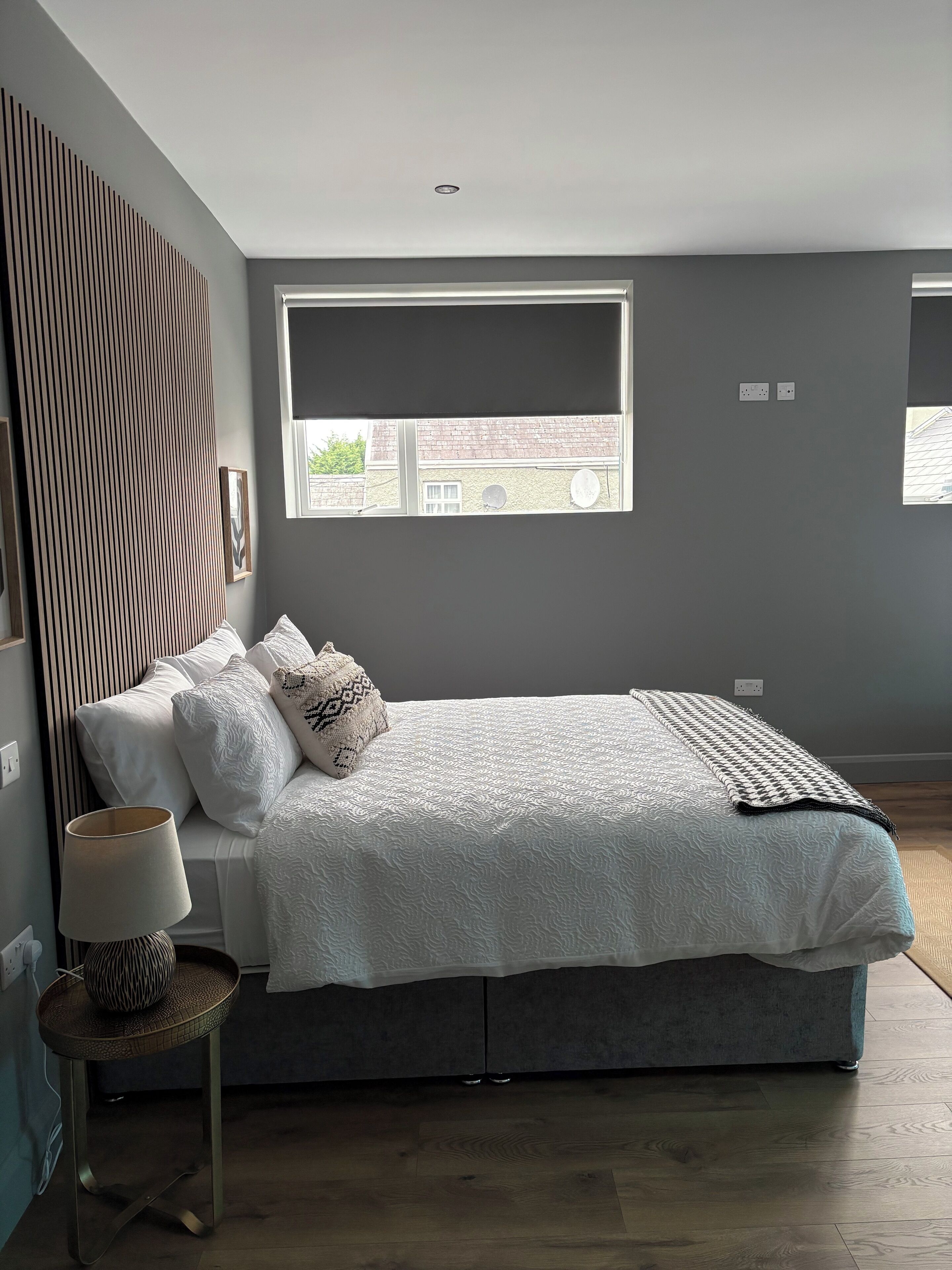 Quarto moderno com cama, abajur e janela com vista para edifícios.