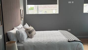 Quarto moderno com cama, abajur e janela com vista para edifícios.