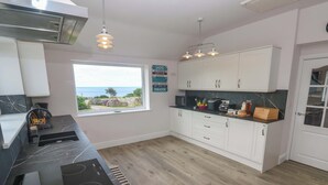 Cozinha moderna com bancada preta, armários brancos e vista para o mar.