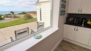 Uma cozinha com vista para o mar, uma pequena área de jantar com cadeiras e um armário com uma placa.