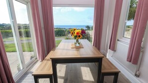 Um quarto com uma mesa de madeira e bancos, um vaso com flores e vista para o exterior por grandes janelas.