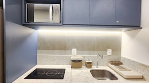 Cozinha moderna com micro-ondas embutido, pia, fogão e lixeira.