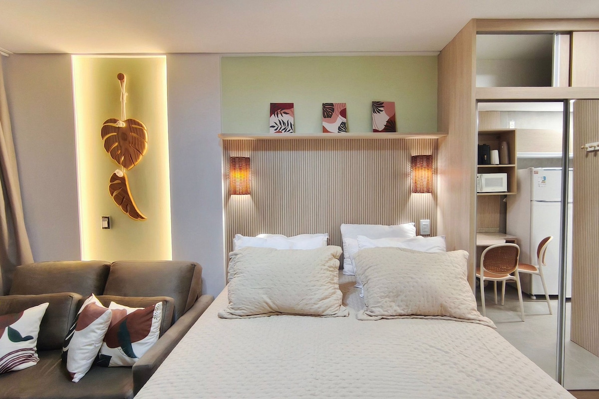 Quarto de hotel com cama, duas mesas de cabeceira, escrivaninha, cadeira, guarda-roupa e obras de arte na parede.