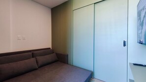 Quarto com sofá, porta deslizante e televisão na parede.