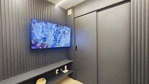 Quarto moderno com televisão de tela plana na parede, painel de madeira escura, uma pequena prateleira com uma xícara e armário com porta deslizante.