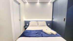 Quarto de hotel com cama, mesas de cabeceira e uma porta, parede azul.