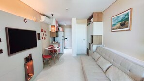Uma sala de estar moderna com televisão de tela plana, um sofá e um espaço de jantar com uma mesa pequena e cadeiras.