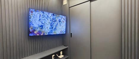 Quarto moderno com televisão de tela plana na parede, painel de madeira escura, uma pequena prateleira com uma xícara e armário com porta deslizante.