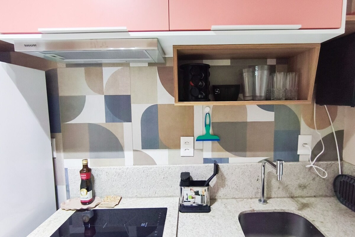 Uma cozinha compacta com micro-ondas, uma pequena estante com utensílios de cozinha, uma garrafa de vinho e uma pia.