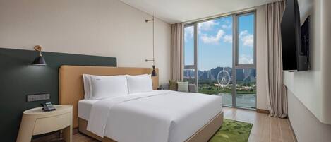 Quarto de hotel com cama, mesa de cabeceira, telefone, televisão e uma grande janela com vista para a cidade.