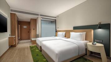 Quarto de hotel com duas camas, uma televisão de tela plana na parede, mesa de cabeceira com abajur e tapete verde.