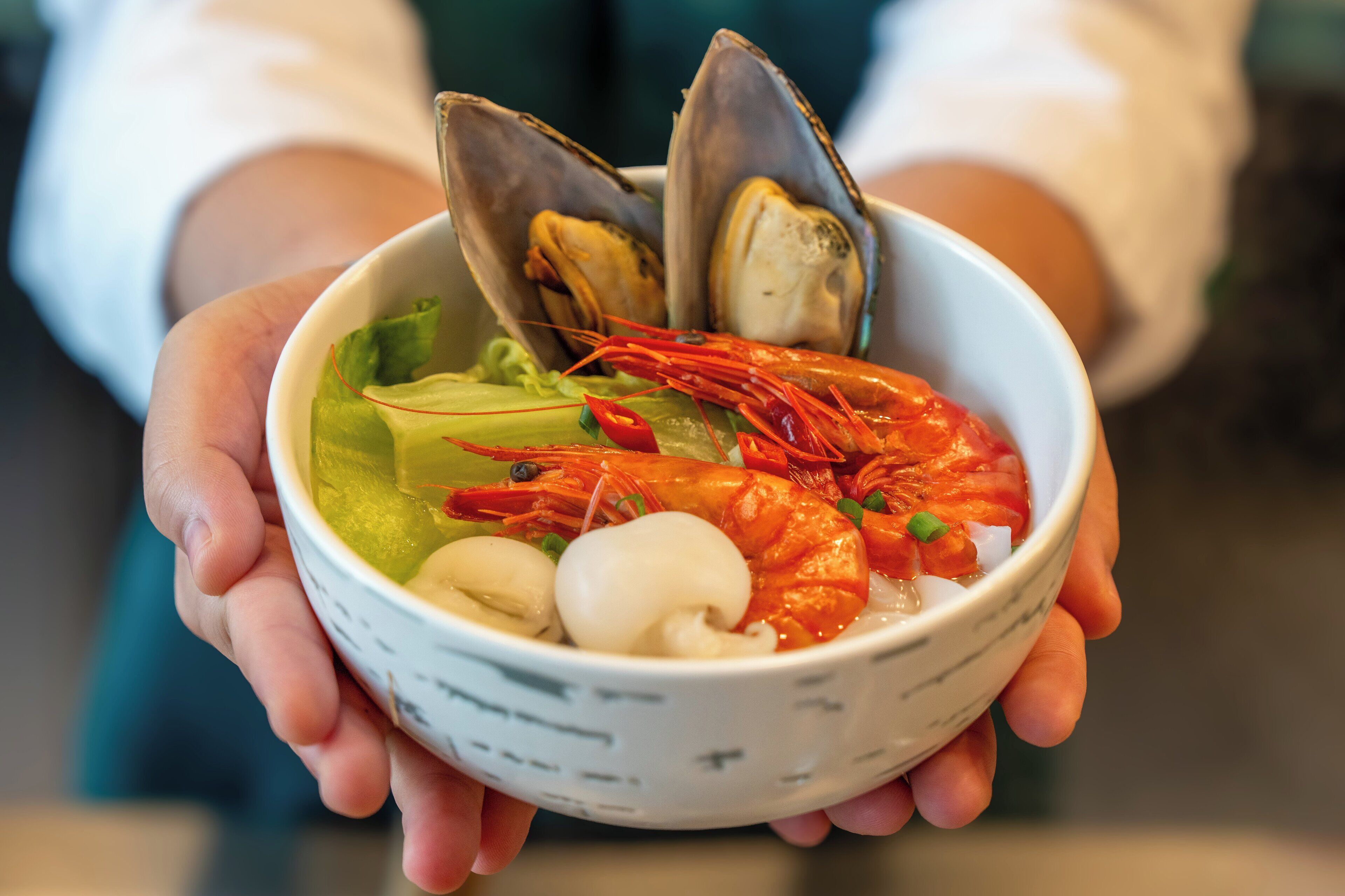 Uma tigela de sopa de mariscos com mexilhões e camarões, segurada por alguém.