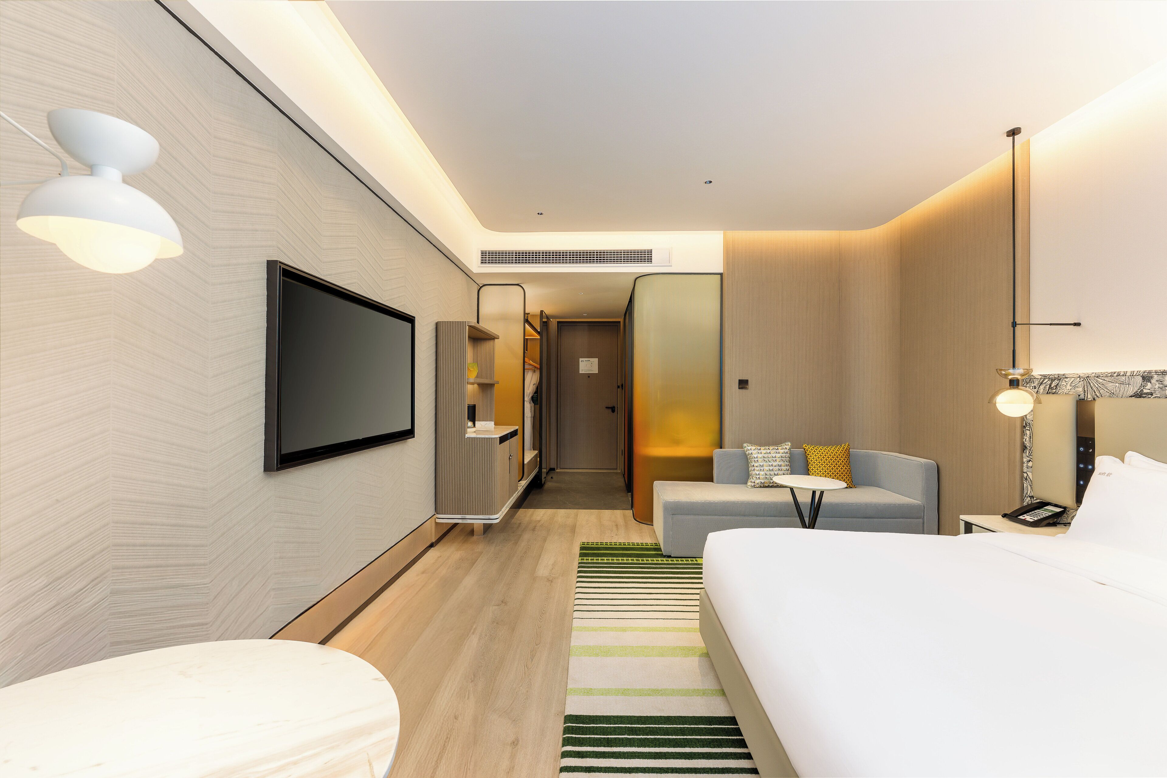 Quarto de hotel moderno com televisão de tela plana, um sofá, uma cama e uma escrivaninha com luminária.