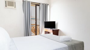 Quarto de hotel com uma cama, televisão sobre uma mesa de madeira e varanda com guarda-corpo.