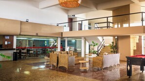 Um hall amplo com mesa de bilhar, móveis de vime e escada que leva a um andar superior.