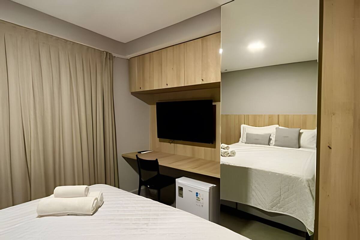 Quarto de hotel com cama, escrivaninha, televisão e minibar.
