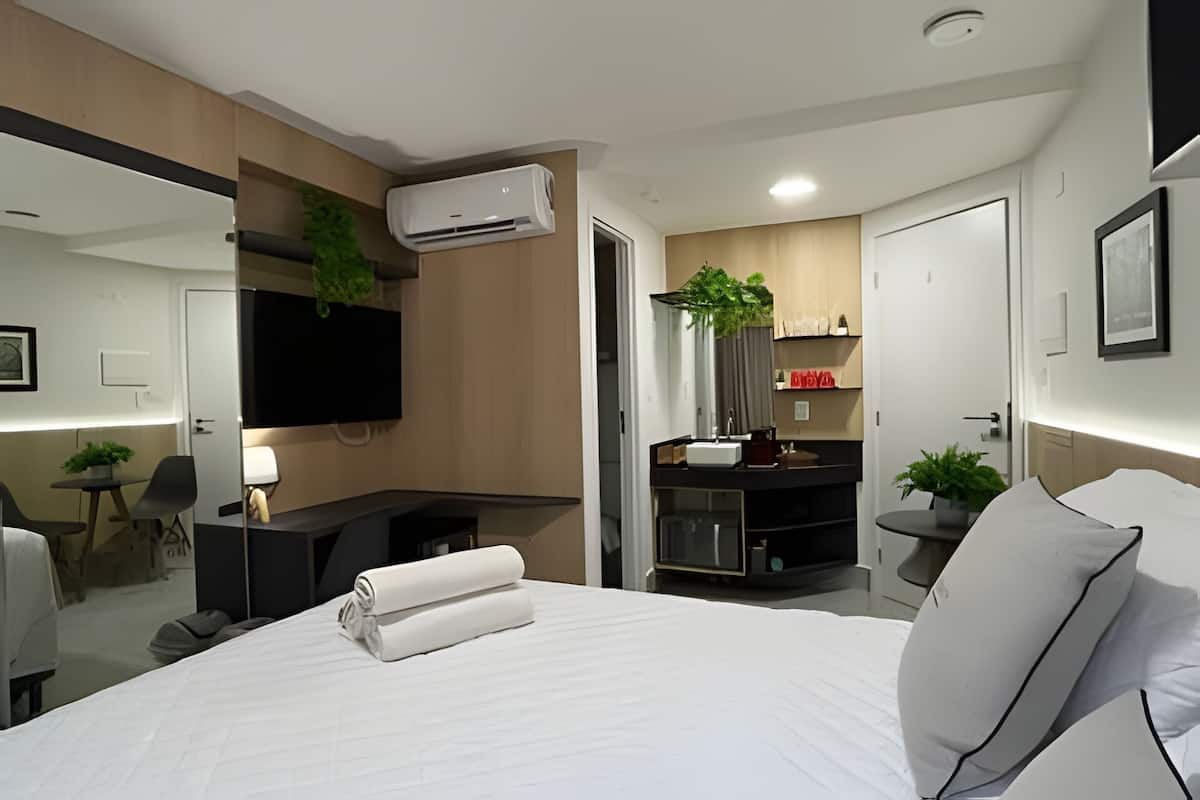 Quarto de hotel moderno com uma cama, uma escrivaninha, uma cadeira, uma TV, um espelho e um banheiro.