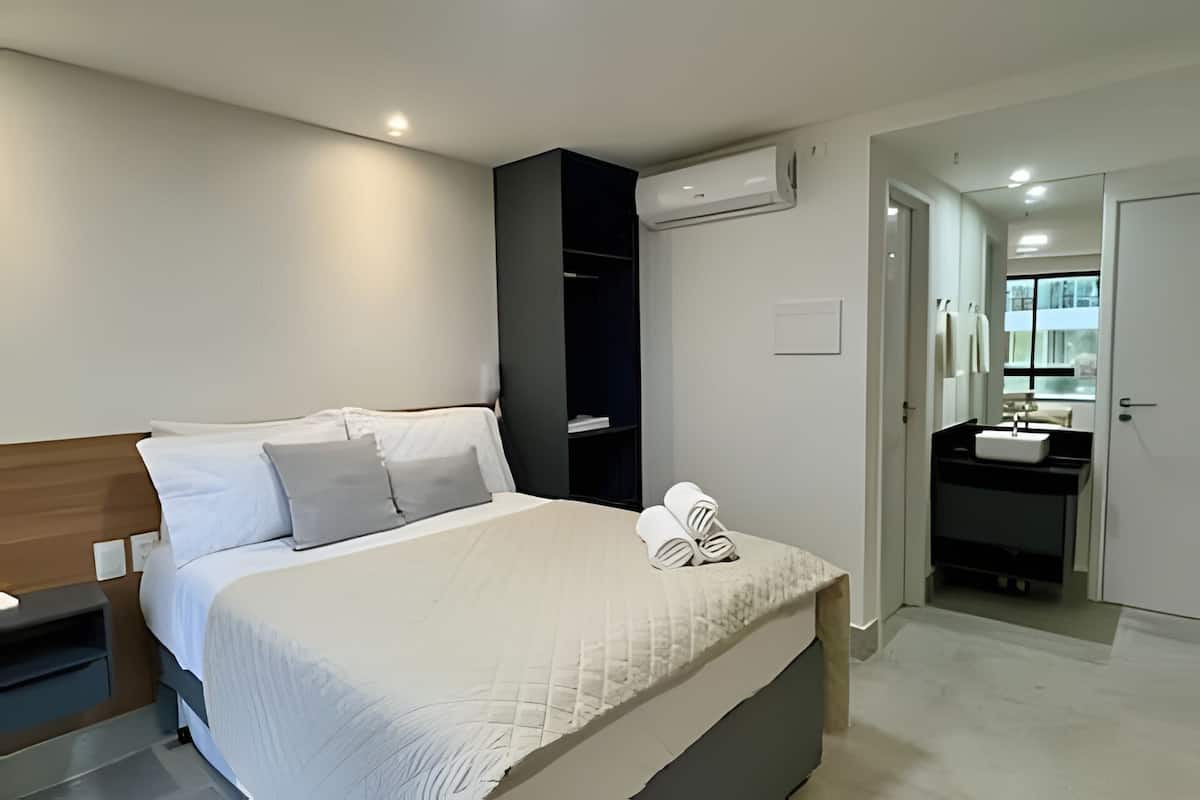 Quarto de hotel com uma cama, um guarda-roupa, ar condicionado, casa de banho com lavatório e espelho.
