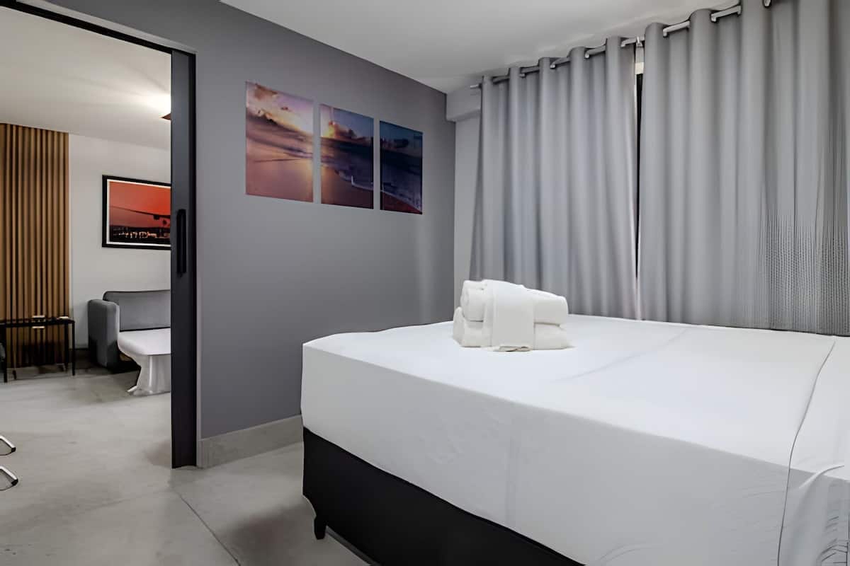 Quarto de hotel com uma cama, uma mesa e uma cadeira. Há três quadros na parede.