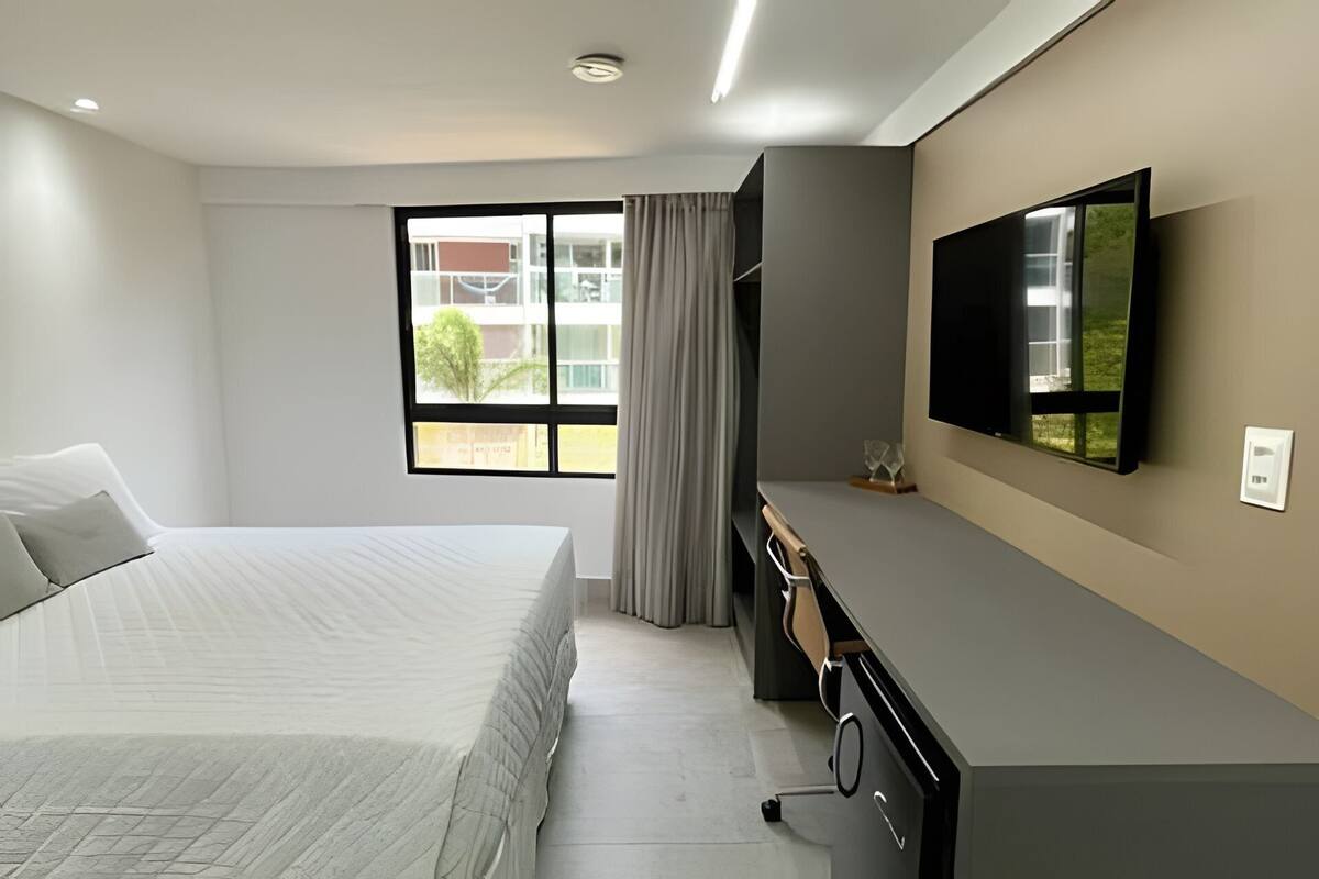 Quarto de hotel moderno com uma cama, uma escrivaninha, uma televisão e uma janela com cortinas.