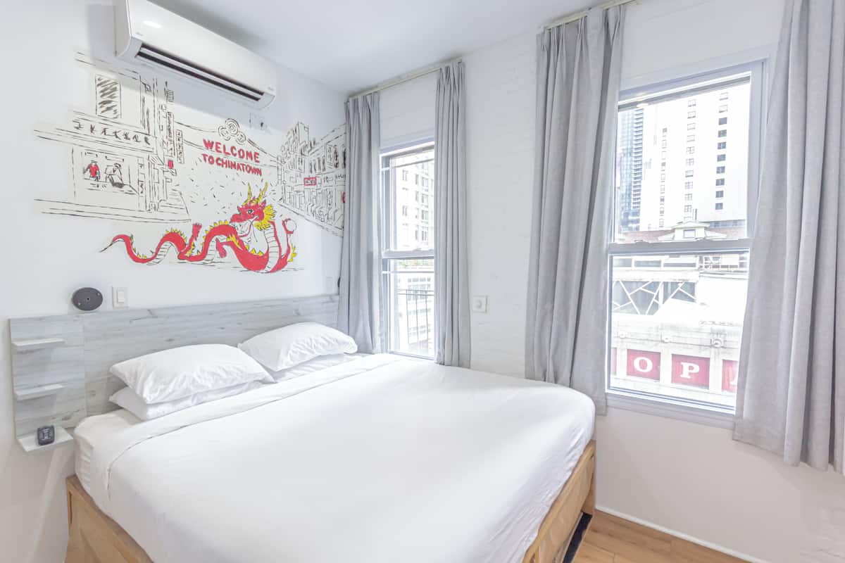 Quarto de hotel moderno com uma cama grande, um mural na parede e uma janela com vista para edifícios.