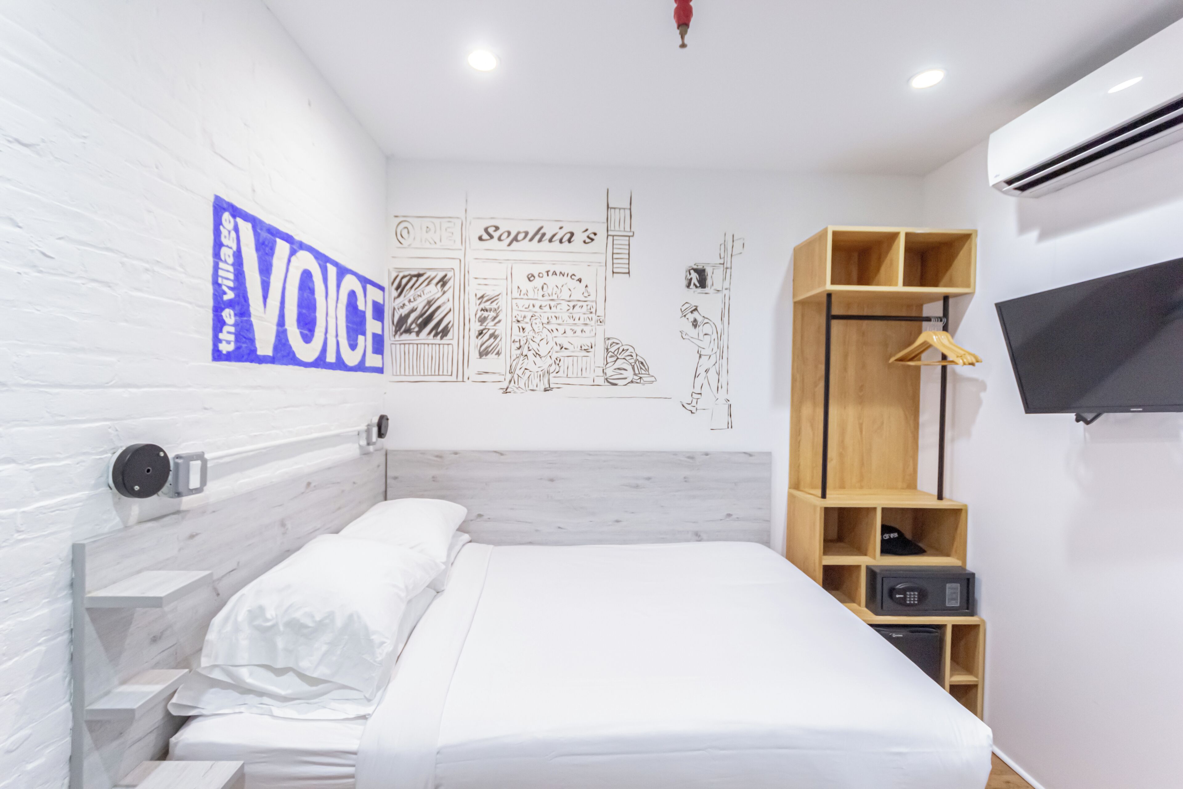 Quarto moderno com cama, televisão fixada na parede, estante de madeira e parede com o letreiro 'VOICE'.