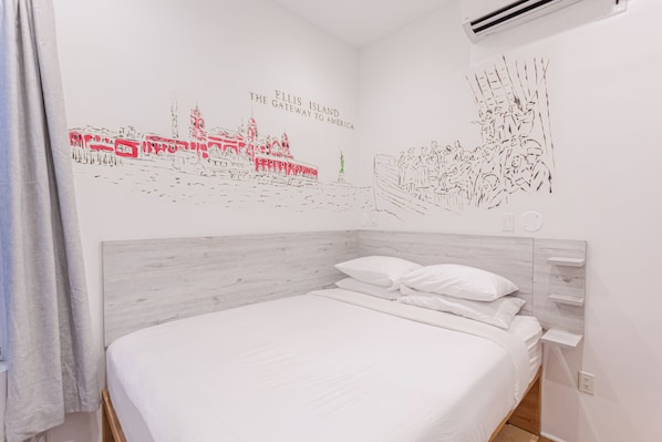 Um quarto com cama, roupa de cama branca, cabeceira de madeira, parede com um desenho em vermelho e preto, e um texto que diz "Ellis Island The Gateway to America".