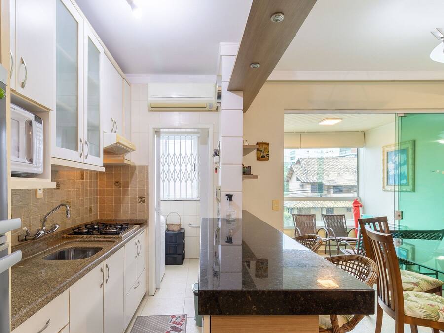 Cozinha moderna com bancada de granito, eletrodomésticos de aço inoxidável e área de jantar com mesa de vidro e cadeiras de madeira.