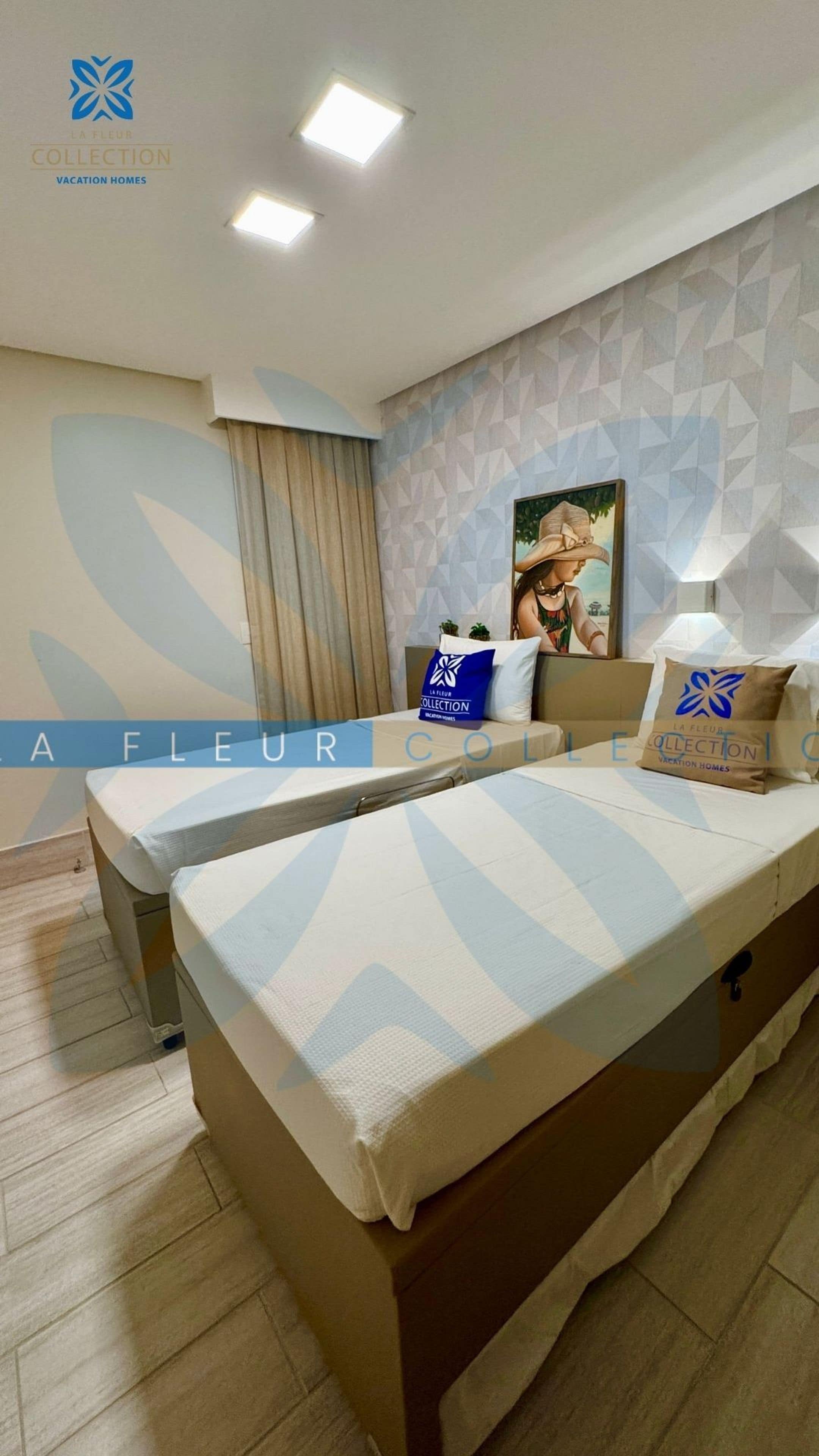 Quarto de hotel com duas camas, parede com padrão geométrico, um quadro e um logotipo na cabeceira.