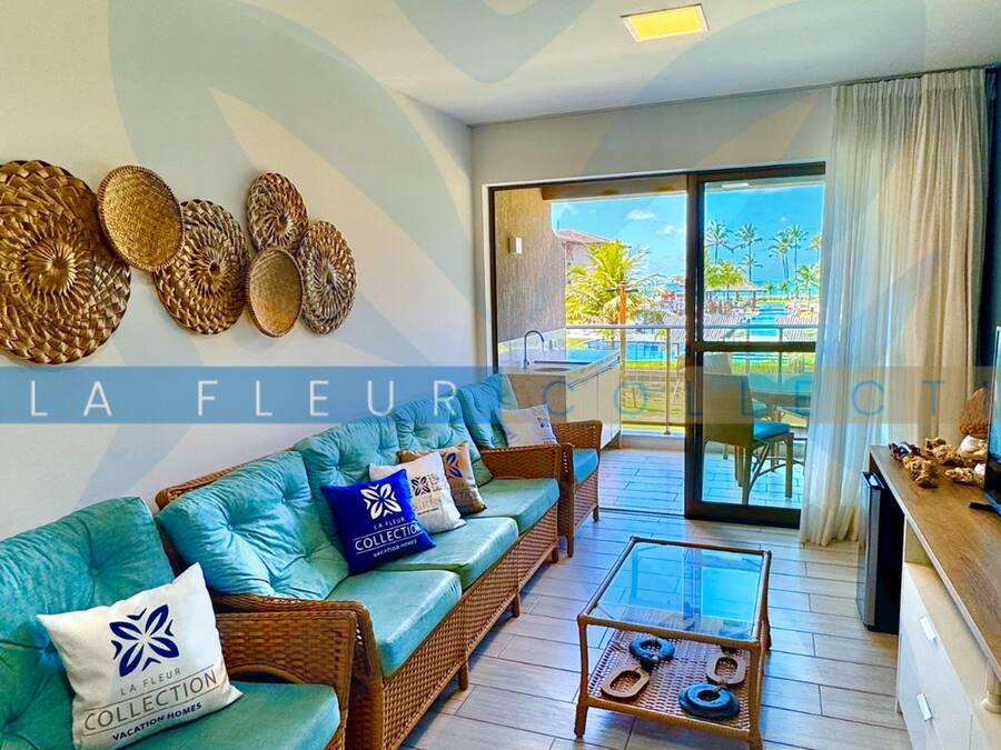 Uma sala de estar espaçosa com um conjunto de sofás, uma mesa de centro e vista para uma piscina e palmeiras.