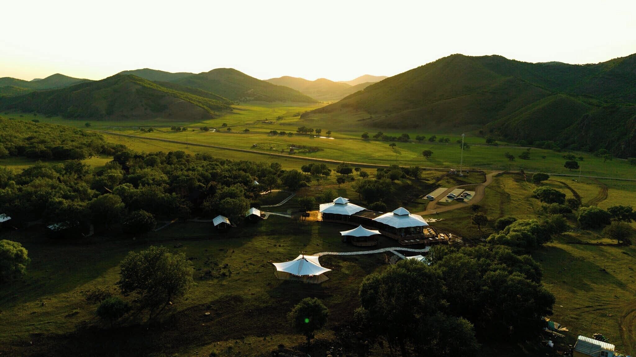 Paisagem rural com várias yurts e um pequeno edifício, rodeado por colinas e campos abertos.