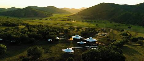 Paisagem rural com várias yurts e um pequeno edifício, rodeado por colinas e campos abertos.
