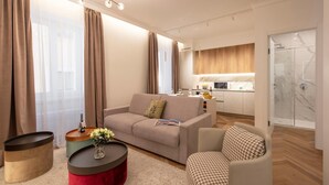 Uma sala de estar moderna com sofá, poltrona e mesa de centro, cozinha ao fundo e área de chuveiro com divisória de vidro.
