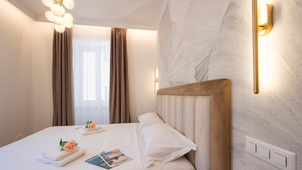 Quarto de hotel com cama, mesa redonda, luminária na parede e janela com cortinas.