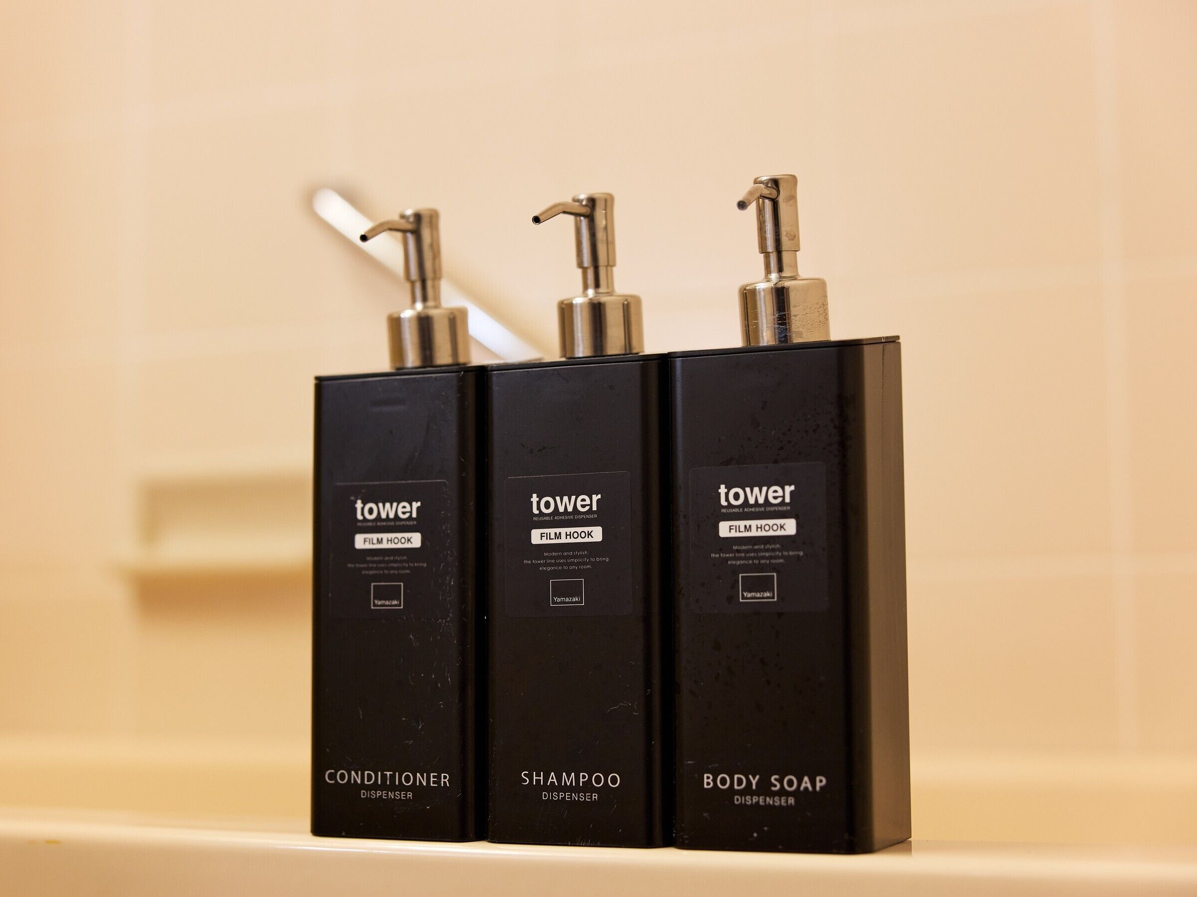 Três dispensadores pretos identificados como 'tower' para condicionador, shampoo e sabonete corporal.