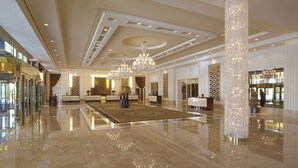 Um hall amplo com piso de mármore polido, um lustre imponente e um balcão de recepção.