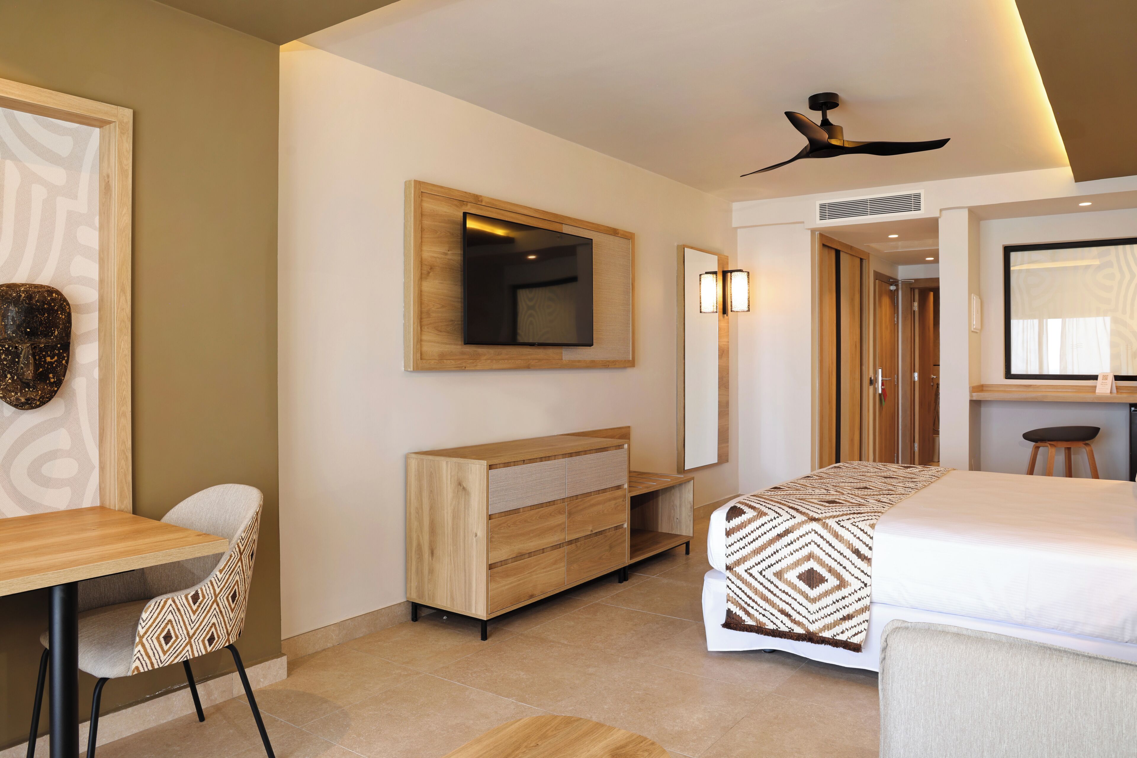 Quarto de hotel moderno com cama, escrivaninha, cadeira, guarda-roupa e ventoinha de teto.