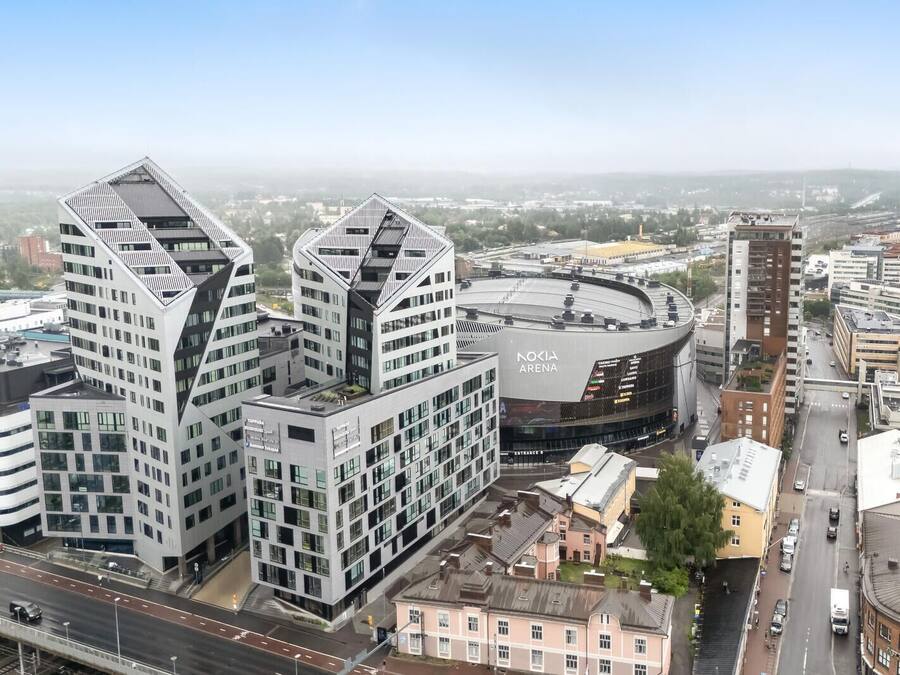 Uma área urbana moderna com um edifício curvo em destaque identificado como 'Nokia Arena' e vários edifícios altos adjacentes.