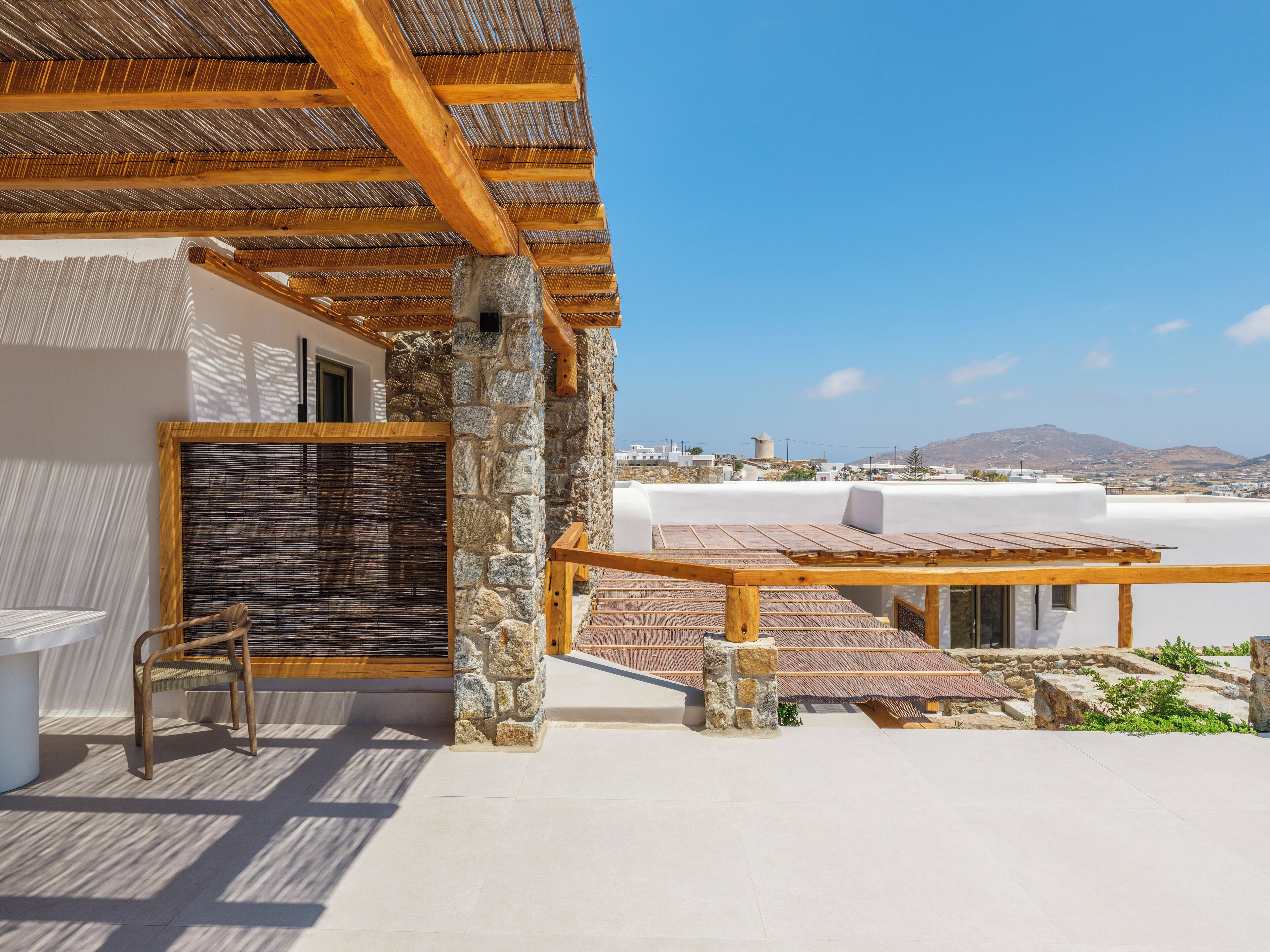 Um terraço no telhado com paredes de pedra, uma pérgola de madeira e vista para a paisagem.