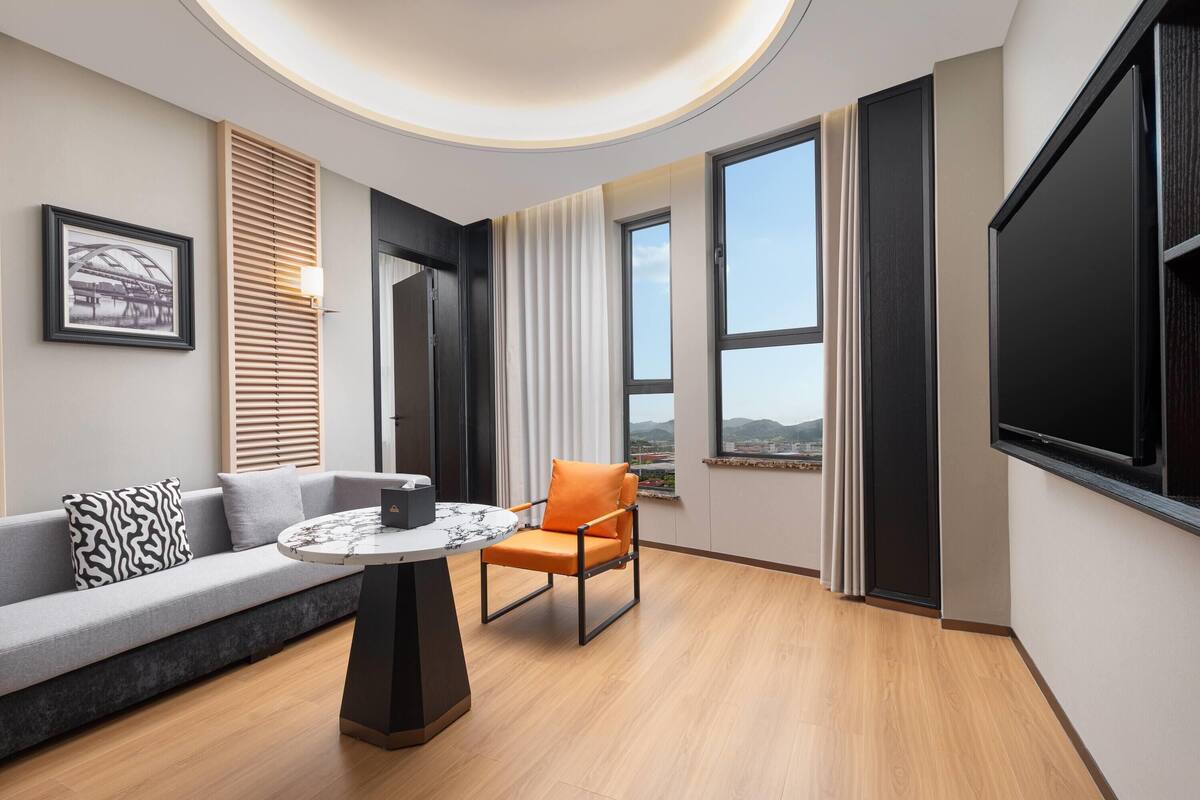 Quarto de hotel moderno com sofá, poltrona, mesa e televisão.