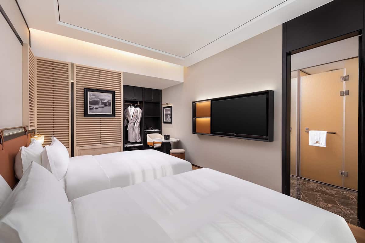 Quarto de hotel com duas camas, televisão, guarda-roupa e porta de casa de banho.