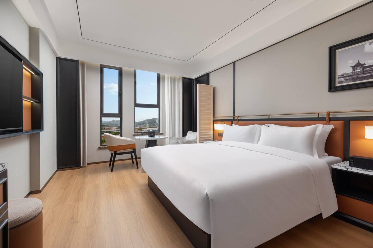 Quarto de hotel com uma cama grande, uma escrivaninha com cadeira, televisão e janela com vista para as montanhas.