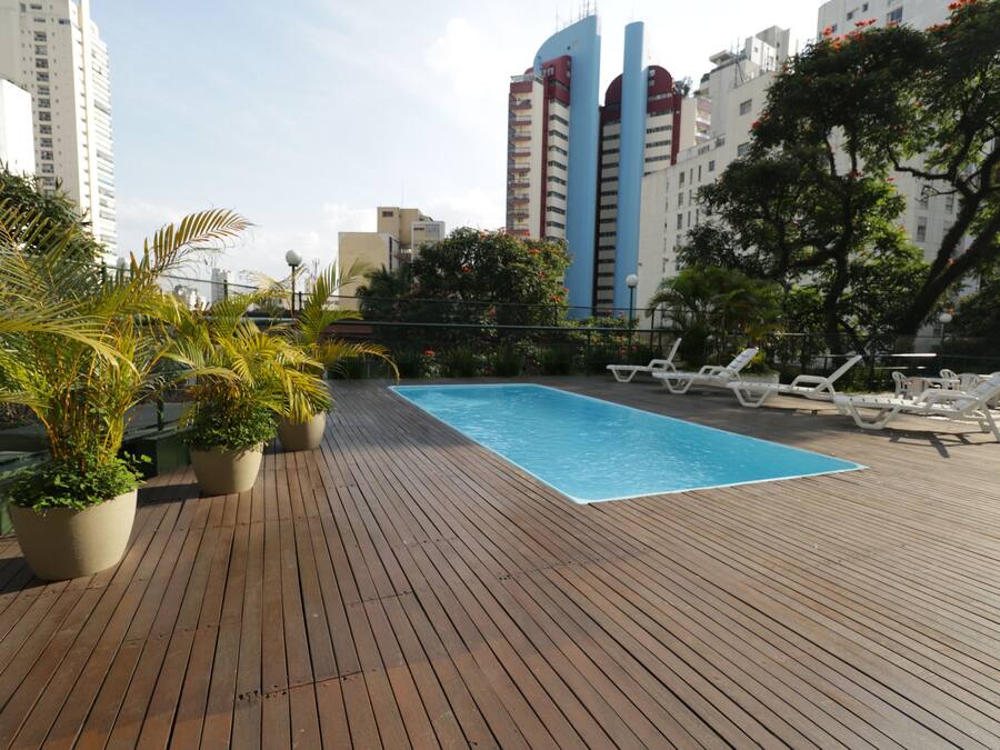 Uma área de piscina no terraço com deck de madeira, espreguiçadeiras e plantas em vasos.