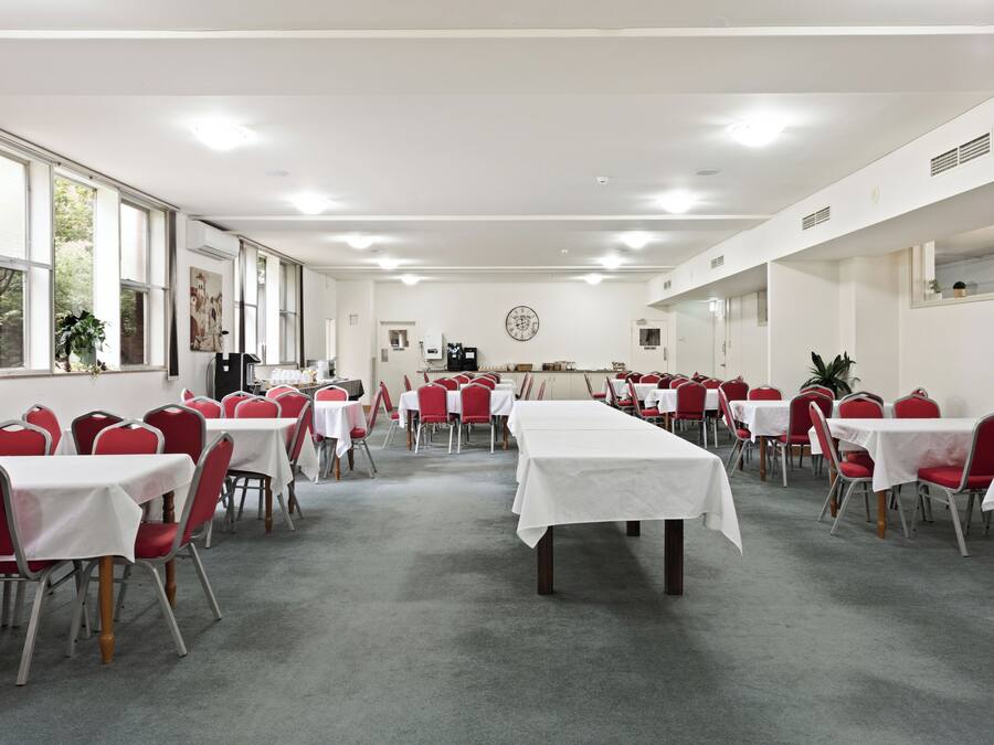 Uma sala de conferências com mesas e cadeiras, janelas amplas e um relógio na parede.