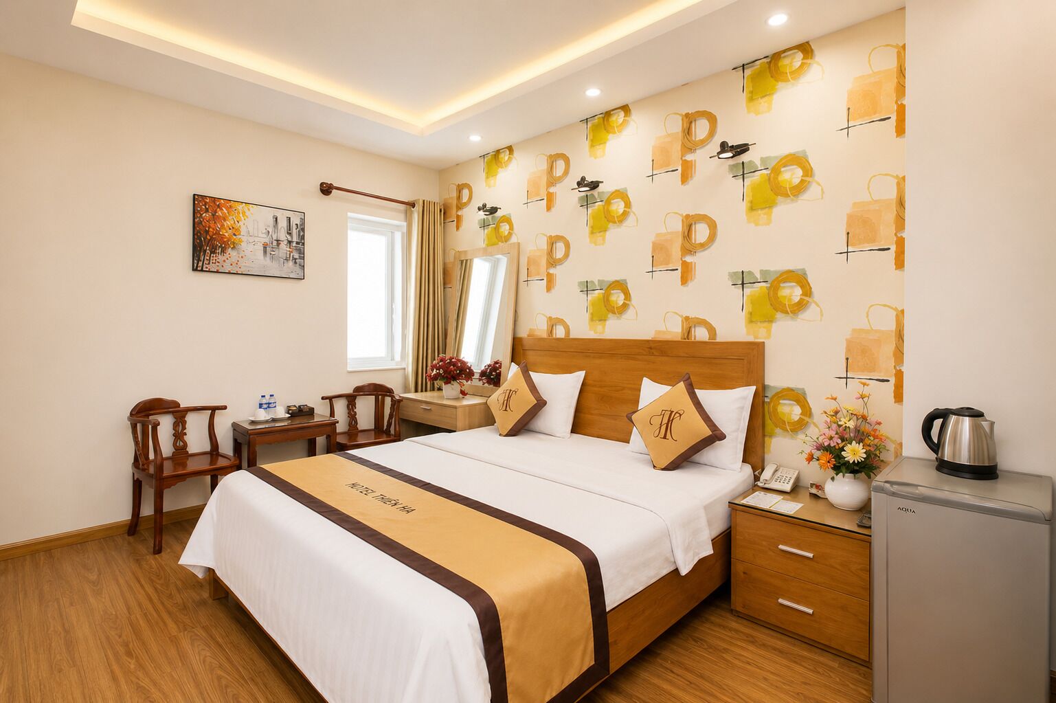 Quarto de hotel com cama, mesa de cabeceira, cadeira, escrivaninha e cozinha compacta.