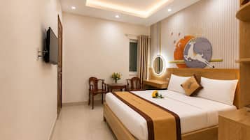 Quarto de hotel com cama, mesa de cabeceira, espelho e uma pequena escrivaninha com cadeiras.