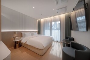 Quarto de hotel moderno com uma cama grande, uma mesa de cabeceira, uma escrivaninha e uma cadeira.
