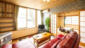 Quarto tradicional japonês com tatames, um sofá vermelho, uma mesa de madeira e uma televisão.